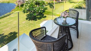 Varanda com mesa e cadeiras de vidro, vista para uma praia e palmeiras.