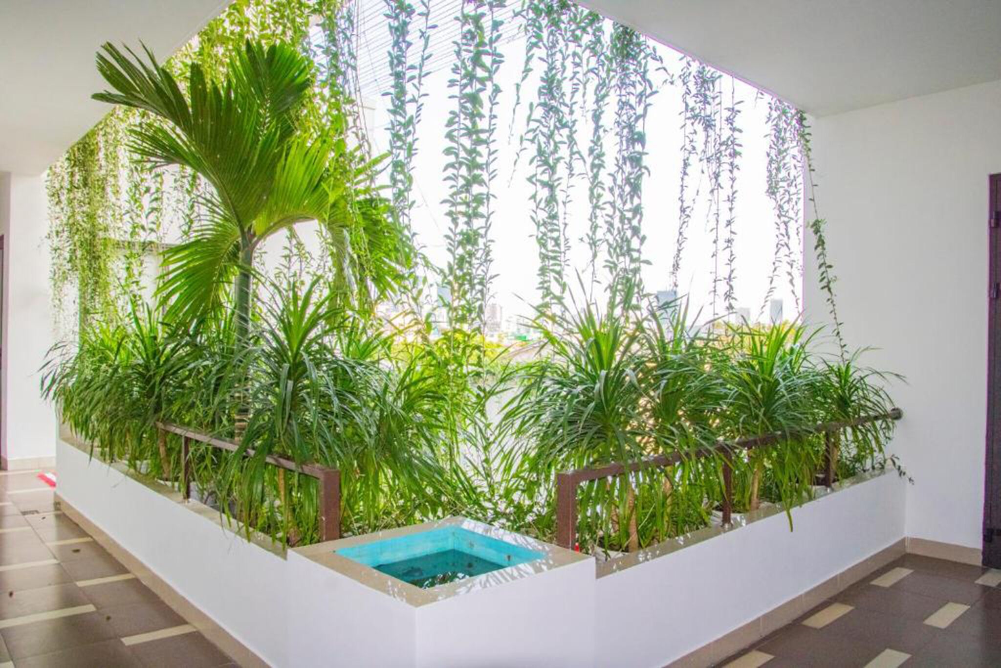 Um átrio interno moderno com uma fonte central, rodeado por vegetação exuberante e jardins verticais.
