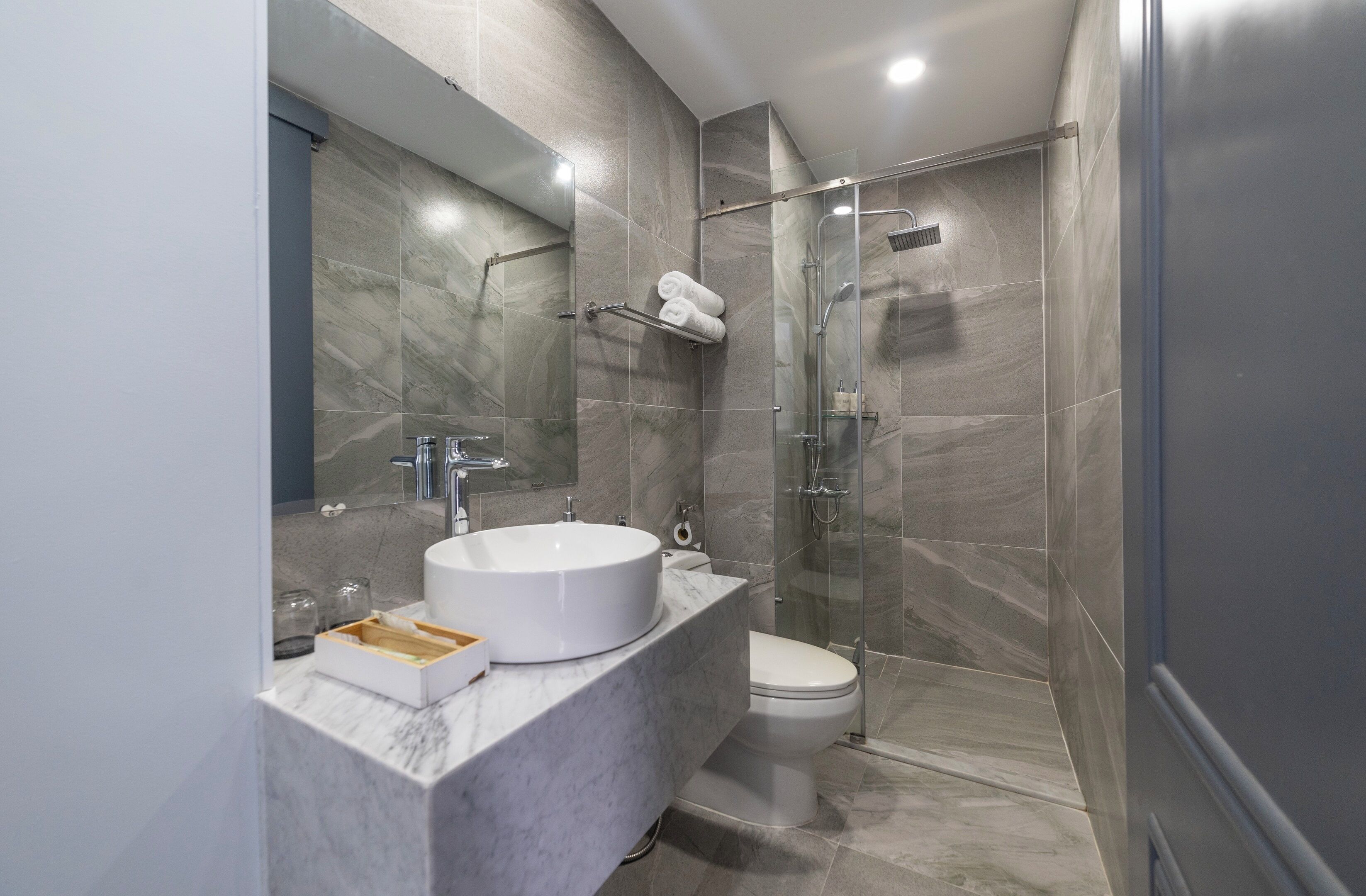 Um banheiro moderno com toucador de mármore, vaso sanitário e chuveiro com parede de vidro.