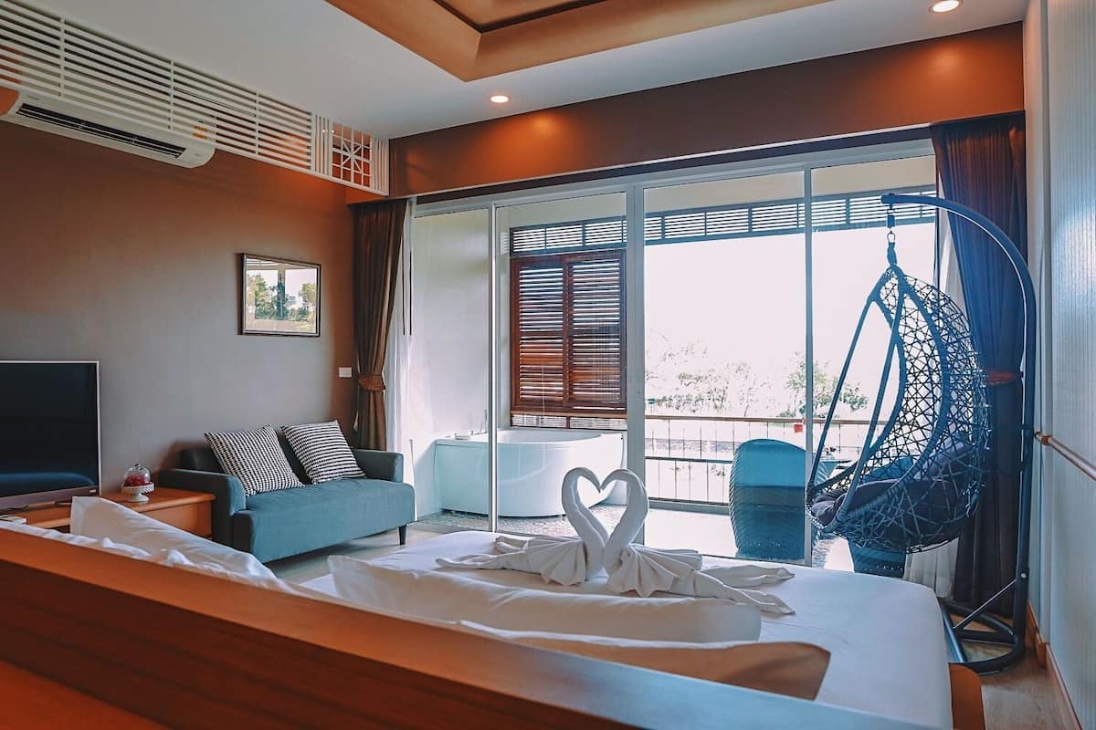 Quarto de hotel com cama, sofá, televisão, janela com persianas e cadeira suspensa.