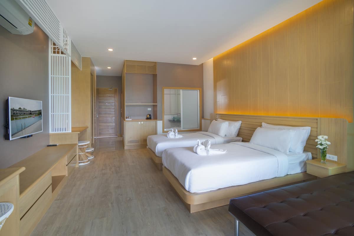 Quarto de hotel moderno com duas camas, um banco de madeira, uma mesinha, uma televisão e um espelho.