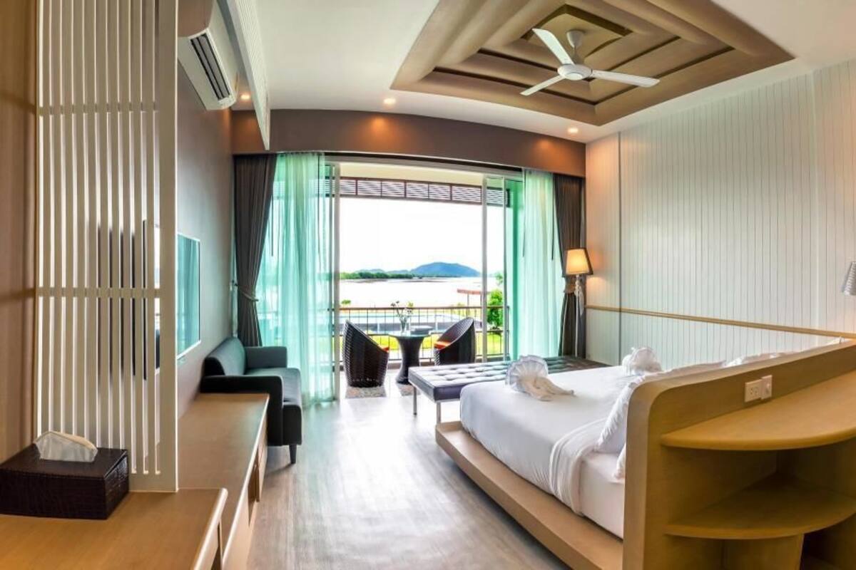 Quarto de hotel com cama, mesa de cabeceira, luminária e vista para uma varanda com área de estar.