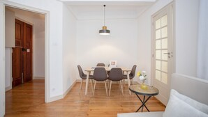 Uma área de refeições com mesa de madeira, seis cadeiras, uma pequena mesa redonda com um vaso e um lustre.