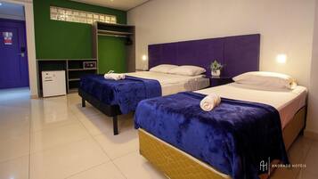 Quarto de hotel com duas camas, um guarda-roupa, uma escrivaninha e um frigorífico pequeno.