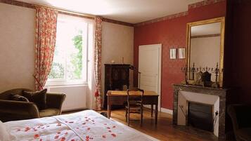 Um quarto com cama, escrivaninha, poltrona, lareira e um espelho grande.