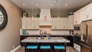 Uma cozinha com ilha central, banquetas, eletrodomésticos de aço inoxidável e iluminação pendente.