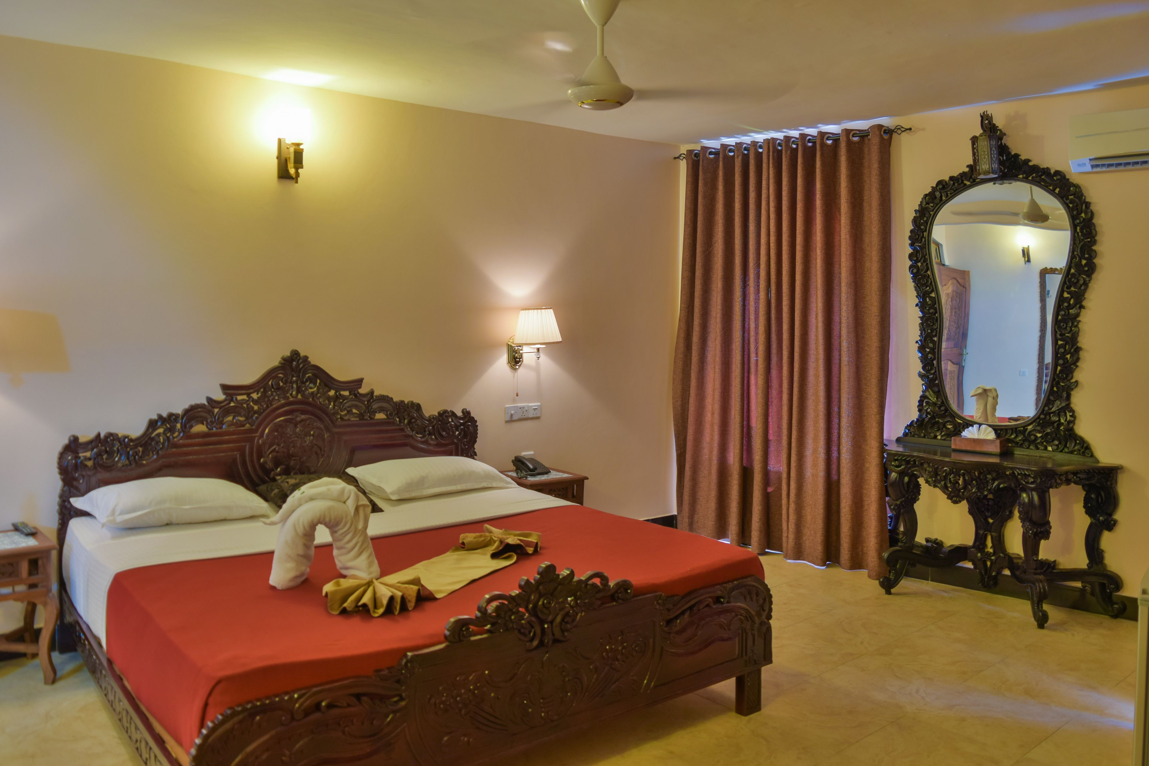 Quarto de hotel com uma cama grande, uma mesa de cabeceira, um espelho e uma cortina.