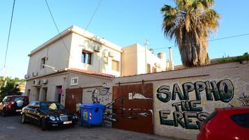 Um edifício com um mural que diz "SAPPHO THE ERES", carros estacionados e uma palmeira.