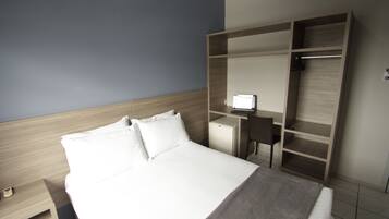 Quarto de hotel com cama, escrivaninha, cadeira e guarda-roupa.