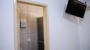 Casa de banho com sanita, lavatório e espelho. Existe uma televisão fixada na parede.