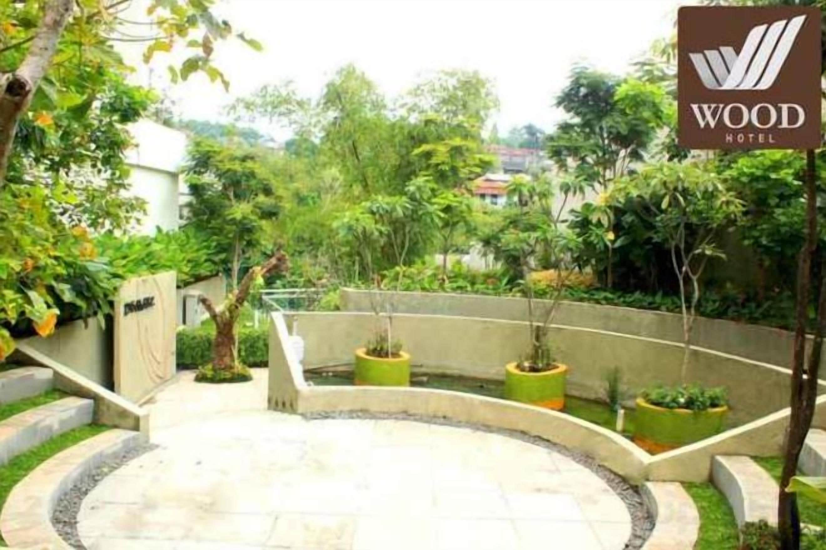 Pátio de hotel com área de estar circular, plantas em vasos e placa indicando Wood Hotel.