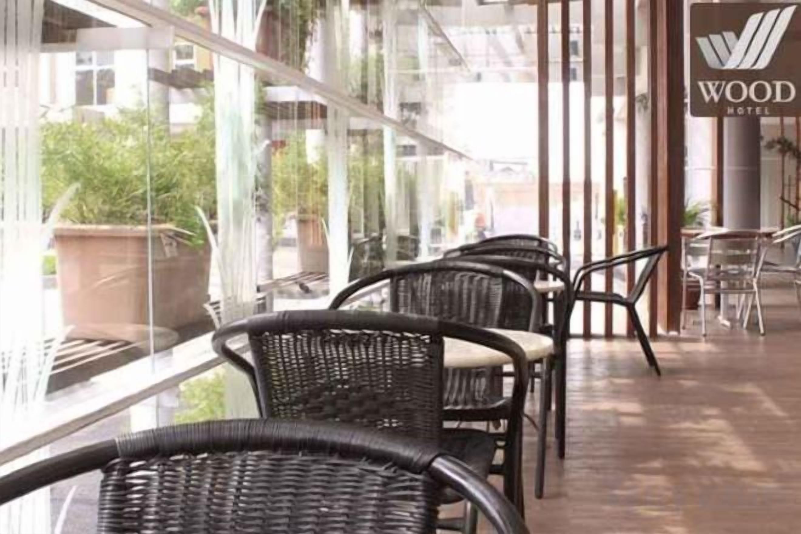 Pátio de hotel com cadeiras de vime, guarda-corpo de vidro e vista para a rua.