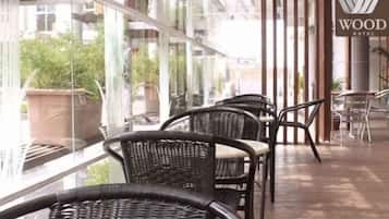 Pátio de hotel com cadeiras de vime, guarda-corpo de vidro e vista para a rua.