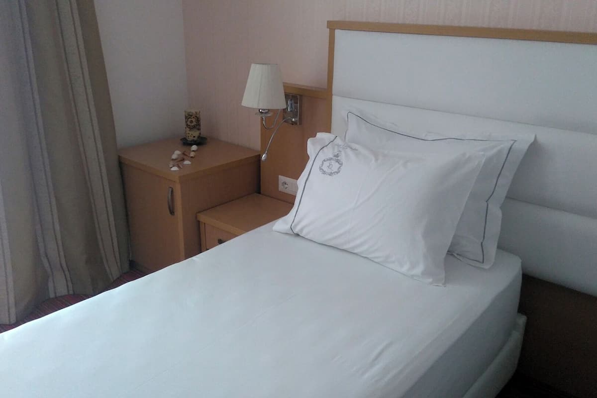 Quarto de hotel com cama, mesa de cabeceira, luminária e arandela.