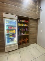 Refrigerador abastecido com diversas bebidas e lanches, incluindo água engarrafada, refrigerantes e salgadinhos.