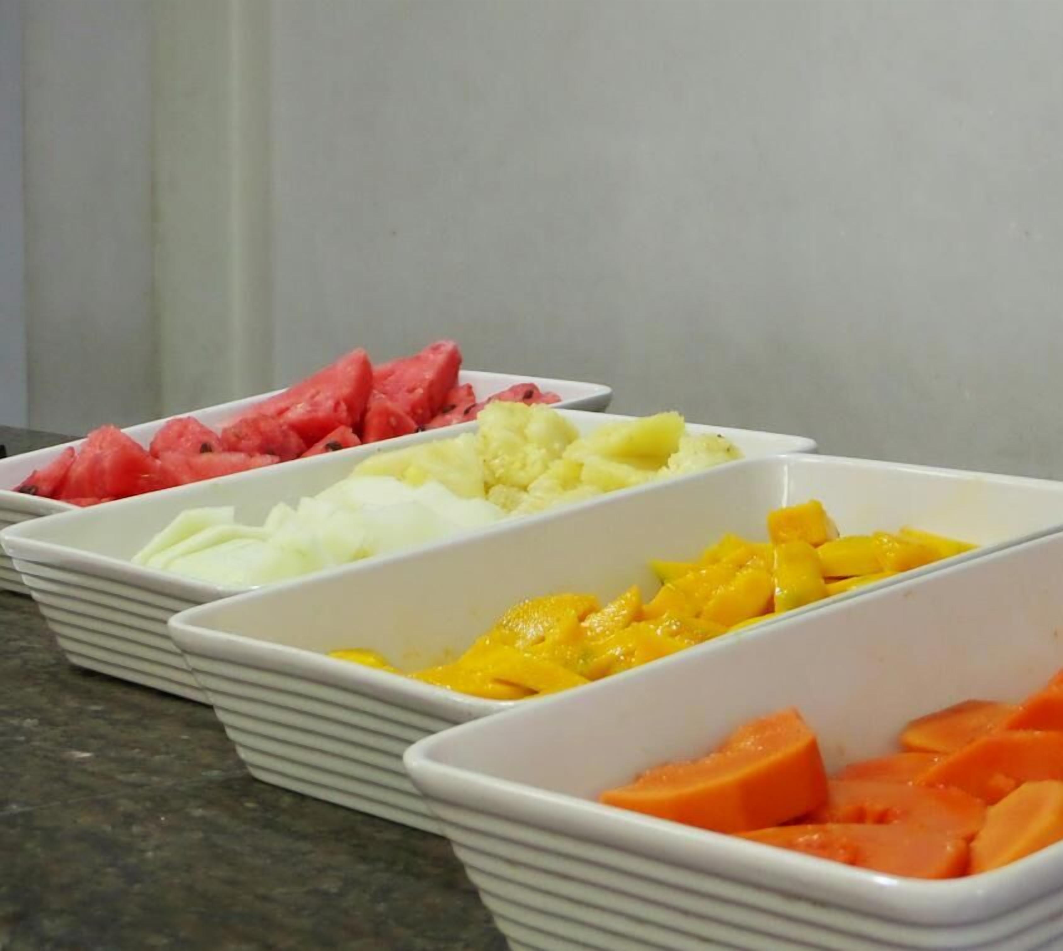 Três bandejas brancas com frutas diferentes: melancia, abacaxi e manga.