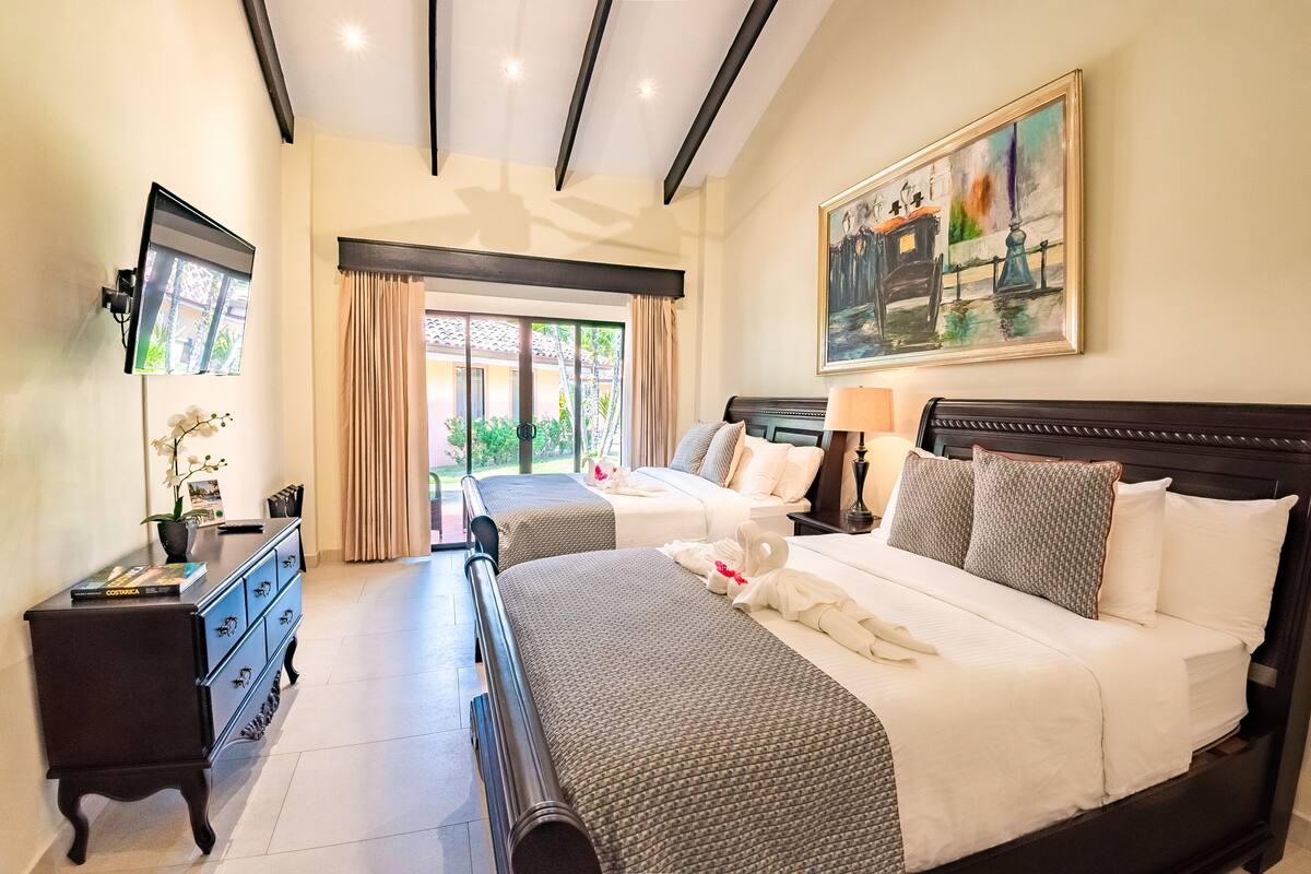 Quarto de hotel com duas camas, uma televisão, cômoda e um quadro.