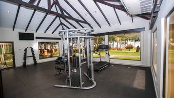 Uma academia com equipamentos de ginástica, grandes janelas e vista para um parque.