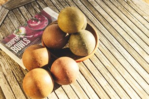 Uma mesa de madeira com uma tigela contendo batatas e uma revista intitulada 'SOUPER BOWLS'.