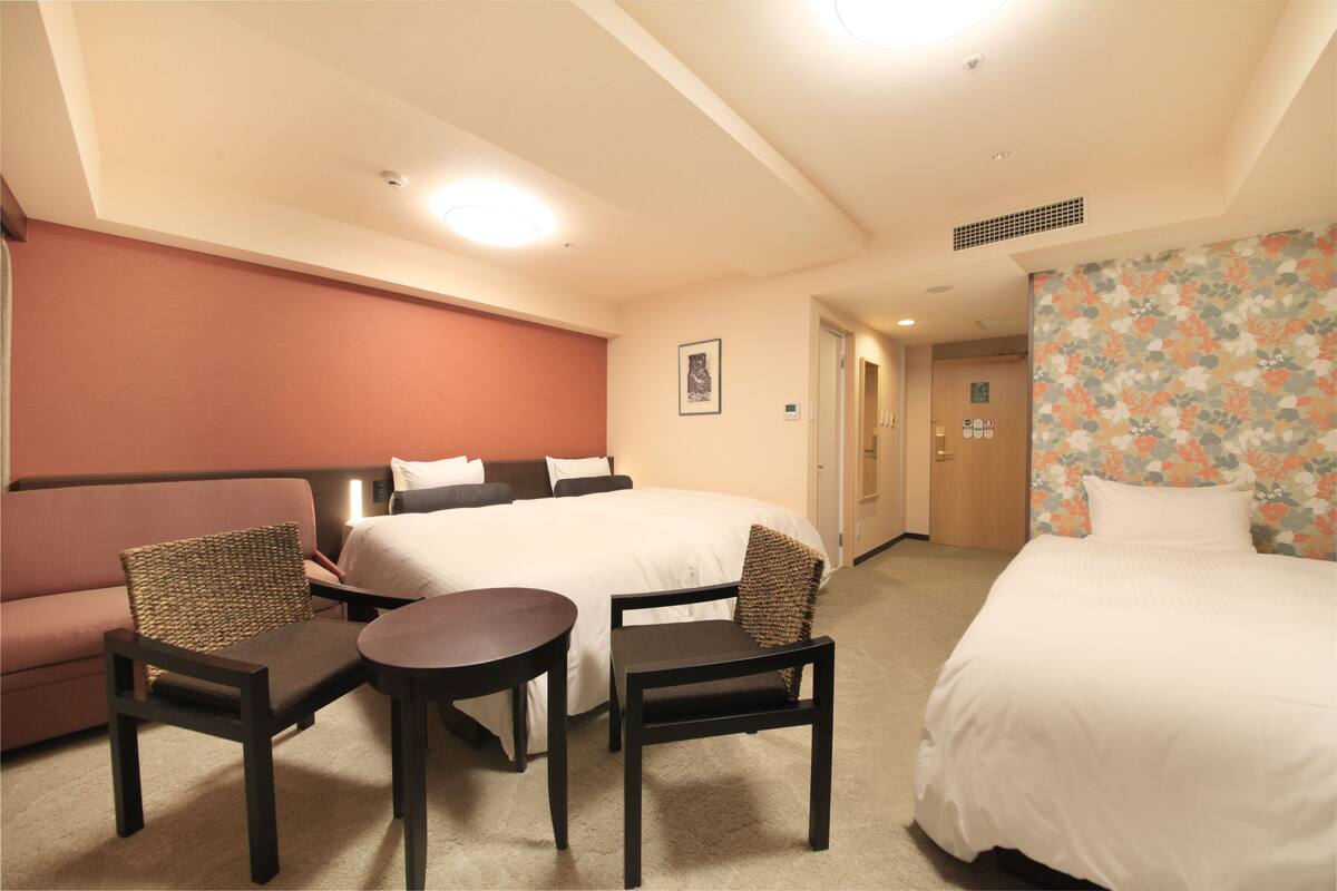 Quarto de hotel com duas camas, um sofá e uma mesinha.