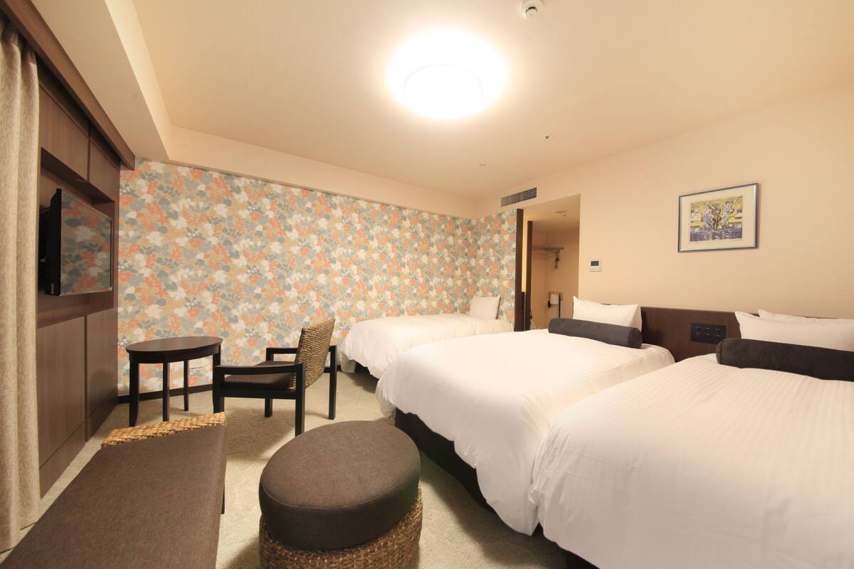 Quarto de hotel com duas camas, uma mesa pequena, uma cadeira e um banco.
