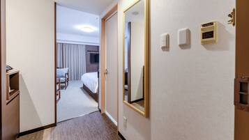 Quarto de hotel com cama, escrivaninha, cadeira, televisão e espelho.