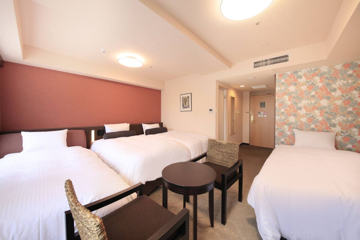 Quarto de hotel com duas camas, uma mesa pequena e uma cadeira.