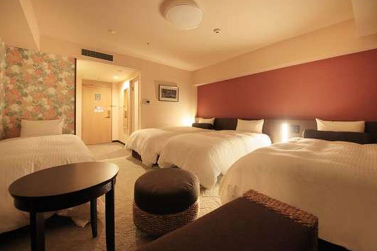 Quarto de hotel com duas camas, uma mesinha e um aquecedor fixado na parede.