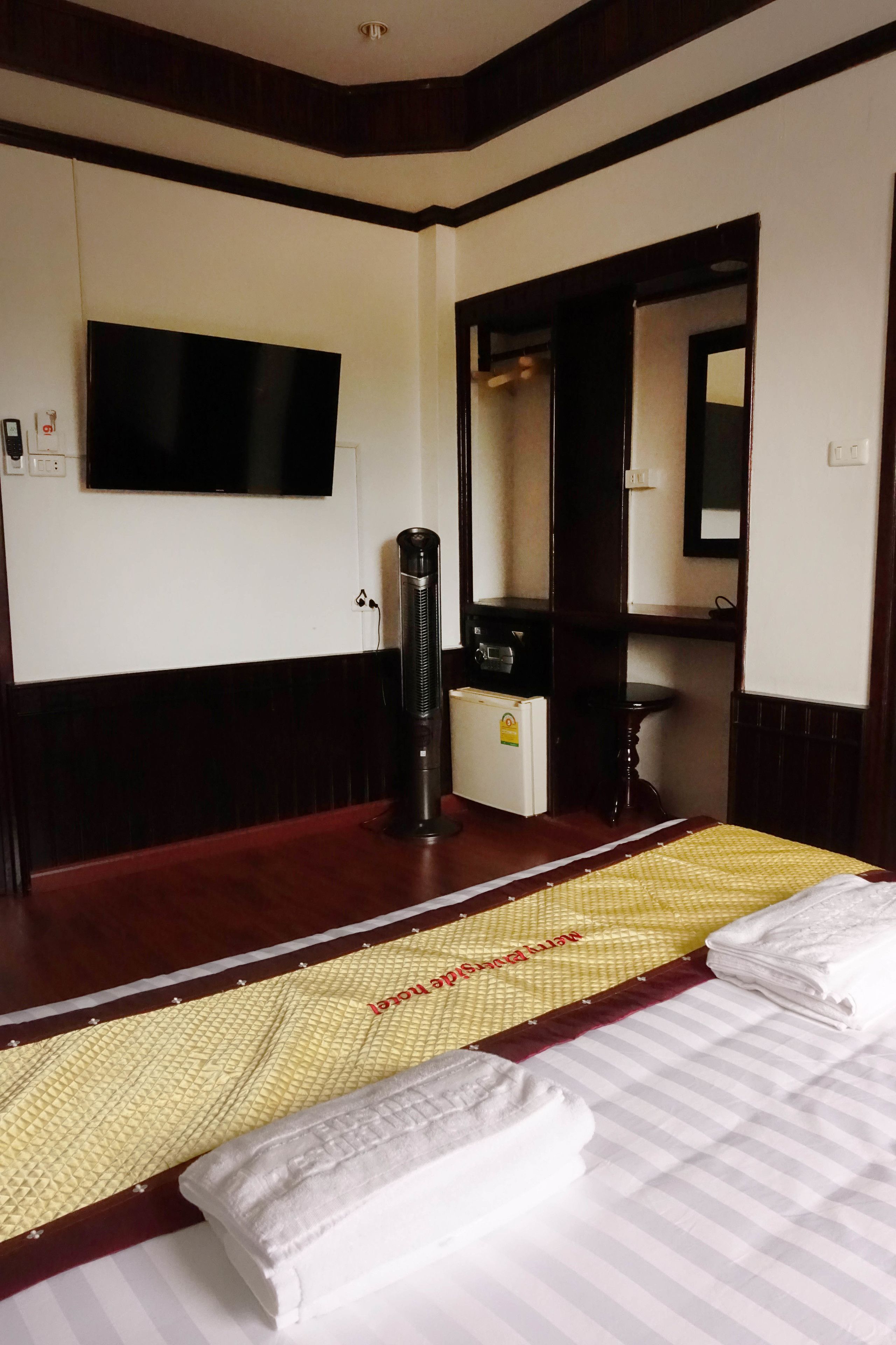Quarto de hotel com uma cama, uma televisão de tela plana na parede, um refrigerador pequeno e um espelho sobre a porta.