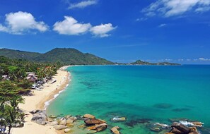 Uma praia com águas azul-turquesa cristalinas, areal arenoso e vegetação exuberante.