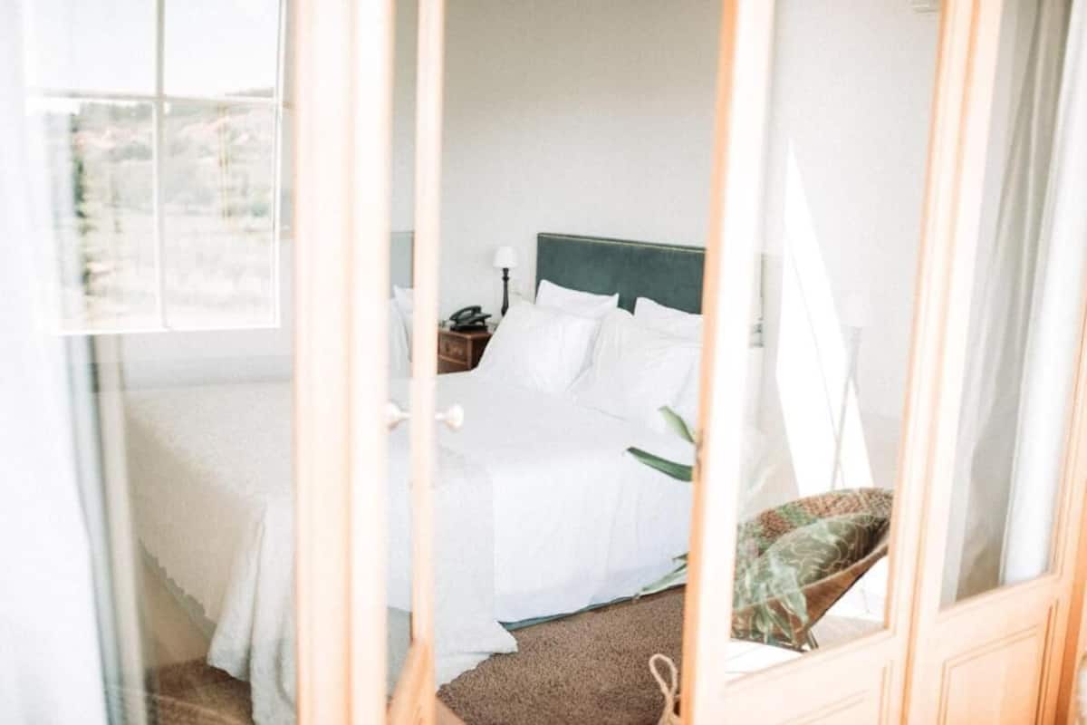 Quarto de hotel com uma cama, mesa de cabeceira, abajur e janela.