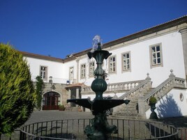 Um pátio com uma fonte, um edifício branco com varanda e uma escadaria.