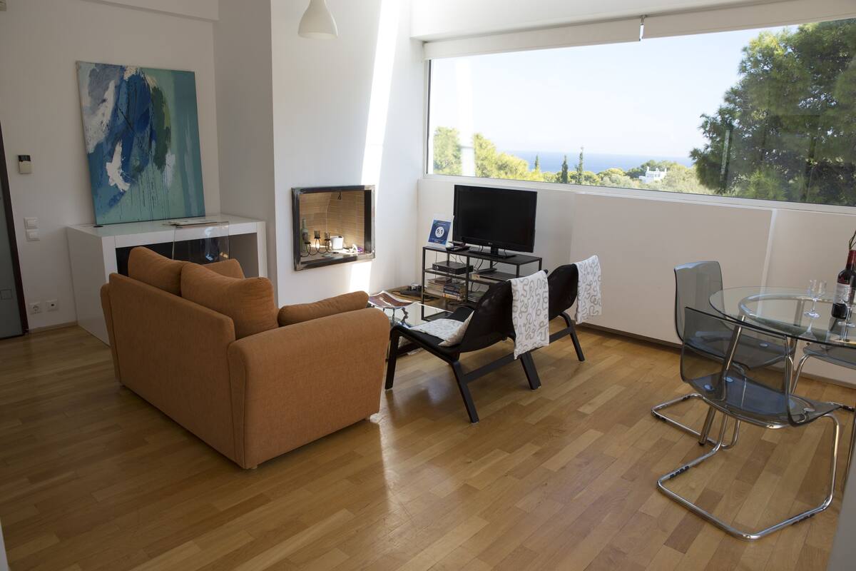 Uma sala de estar moderna com sofá, mesa de centro de vidro, televisão e área de jantar com mesa e cadeiras de vidro.
