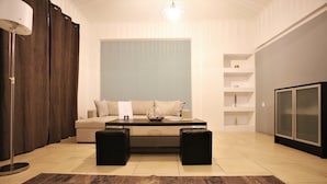 Uma sala de estar moderna com um sofá, dois pufes pretos, uma mesa de centro, um tapete estampado, um abajur, um painel decorativo na parede e estantes embutidas com um armário.