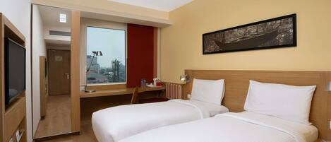 Quarto de hotel com duas camas, uma escrivaninha, televisão e vista para a cidade.