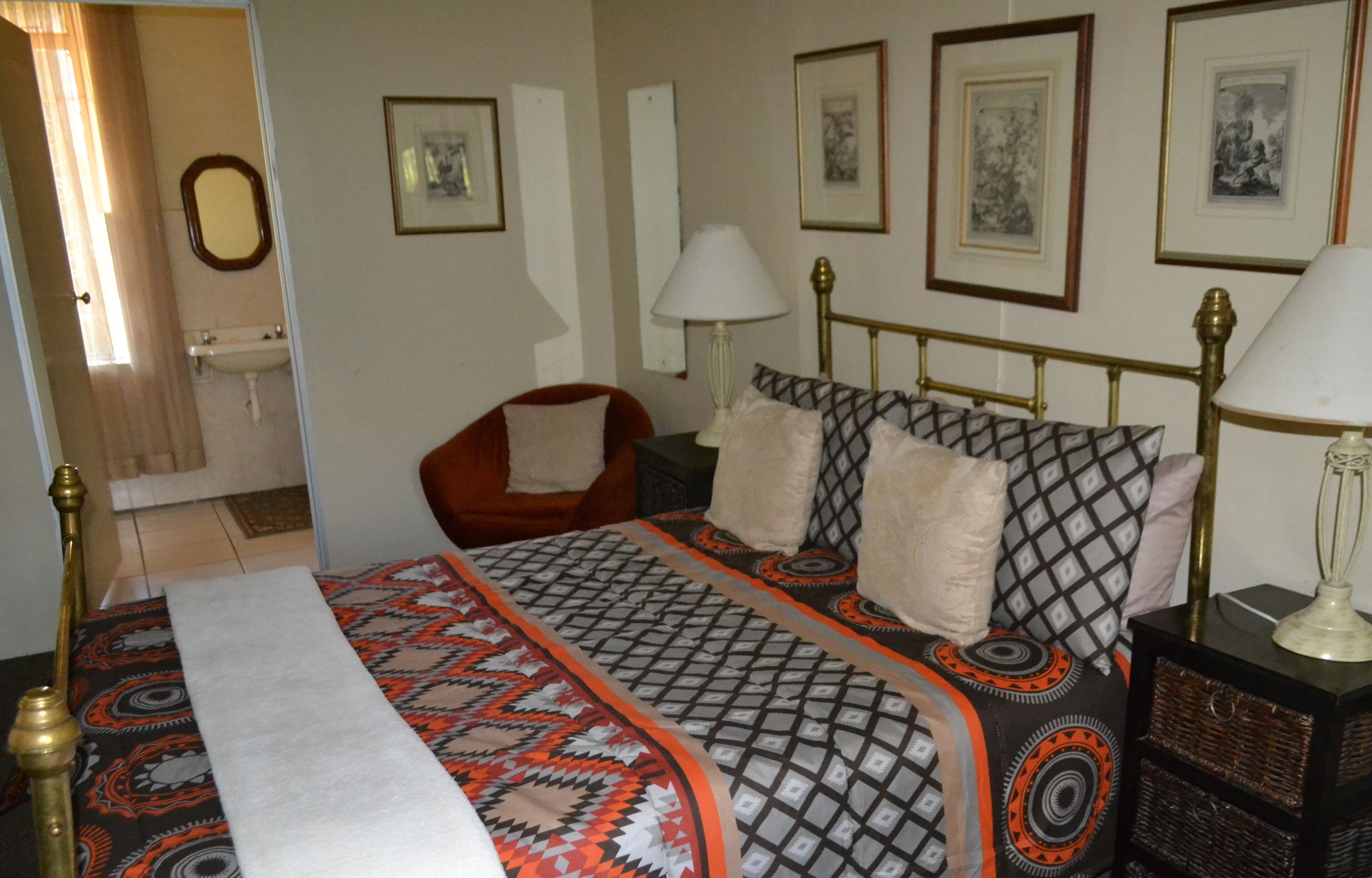 Quarto com cama, cadeira, mesa de cabeceira, abajur, espelho e quadros na parede.