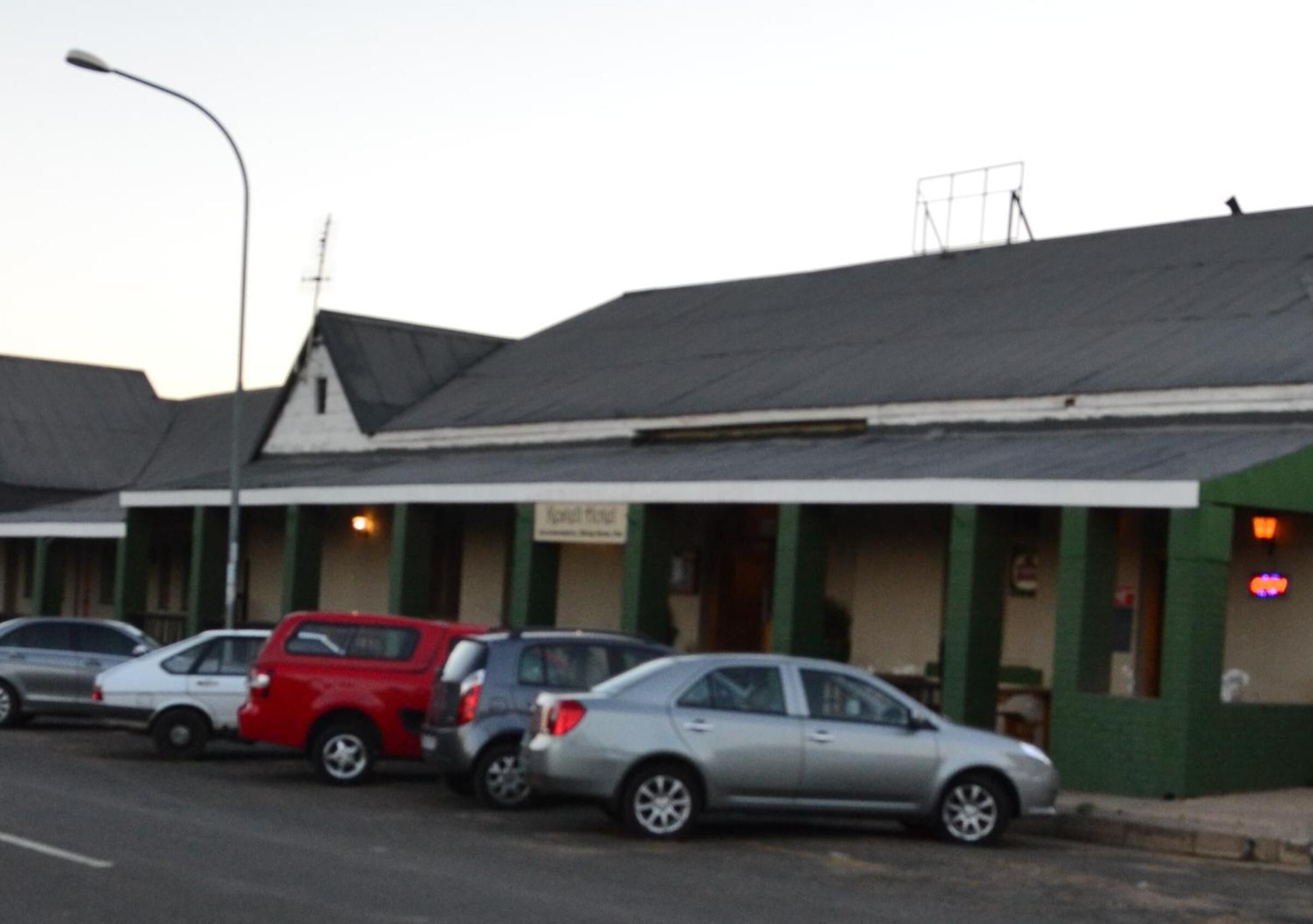 Uma fila de carros estacionados em frente a um edifício com fachada verde e uma placa que diz 'Hotel'.