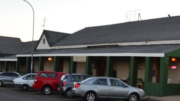 Uma fila de carros estacionados em frente a um edifício com fachada verde e uma placa que diz 'Hotel'.