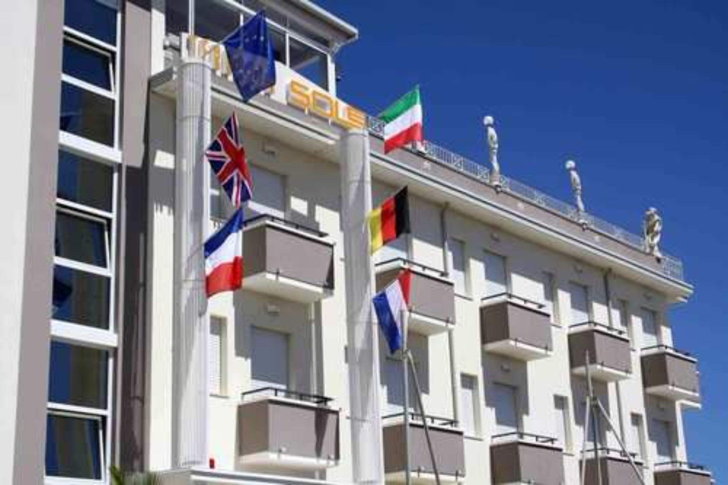 Um edifício com vários andares, varandas e bandeiras, incluindo as bandeiras do Reino Unido, França e Emirados Árabes Unidos.