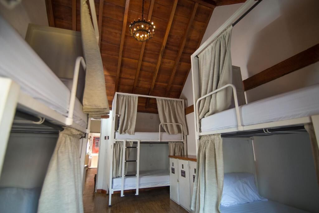 Quarto com beliches, tetos de madeira e um candelabro. Há beliches em ambos os lados e um pequeno armário com escada.