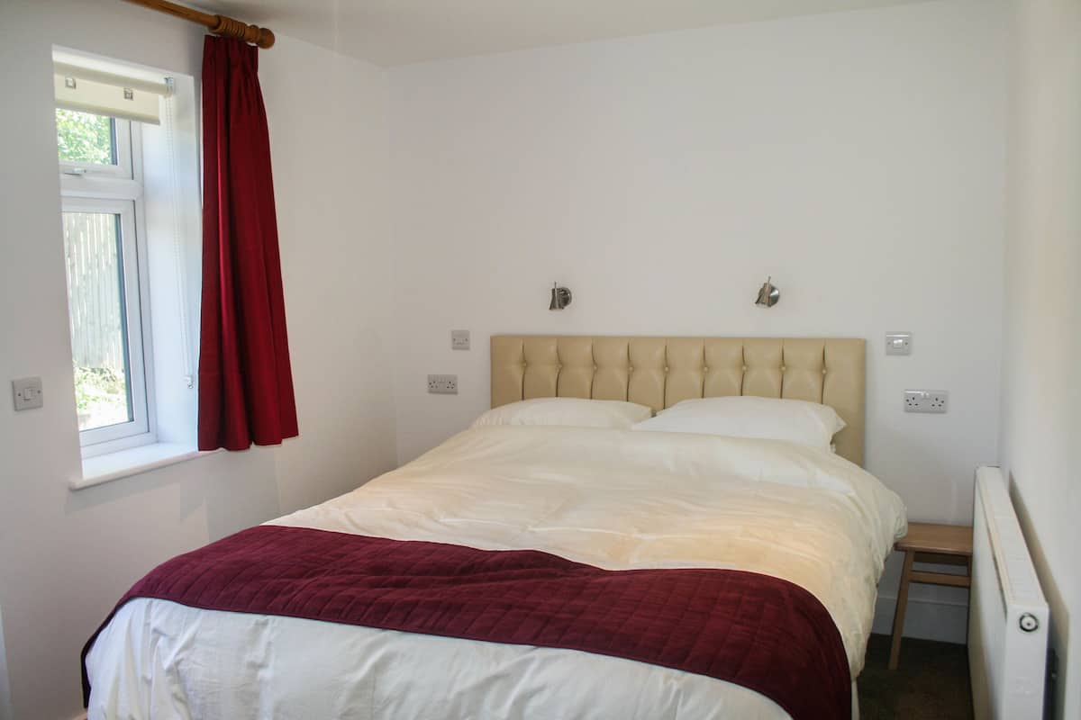 Quarto com cama, janela com cortinas, radiador e uma pequena mesa.