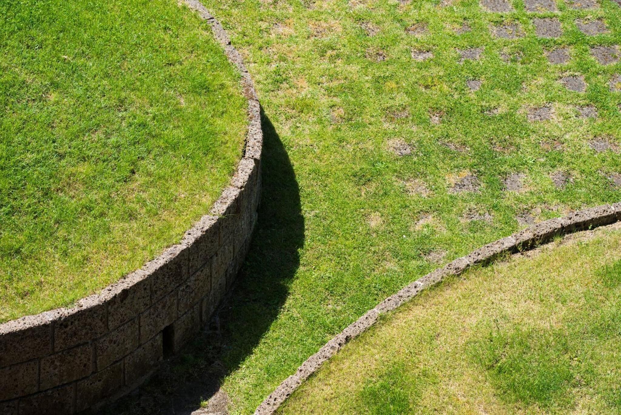 Muro de pedra com uma área gramada ao lado.