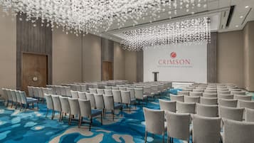 Sala de conferências com fileiras de cadeiras, carpete azul e teto branco com luminárias pendentes. Uma tela exibe o texto “CRIMSON RESORT & SPA BORACAY ISLAND | STATION ZERO”.