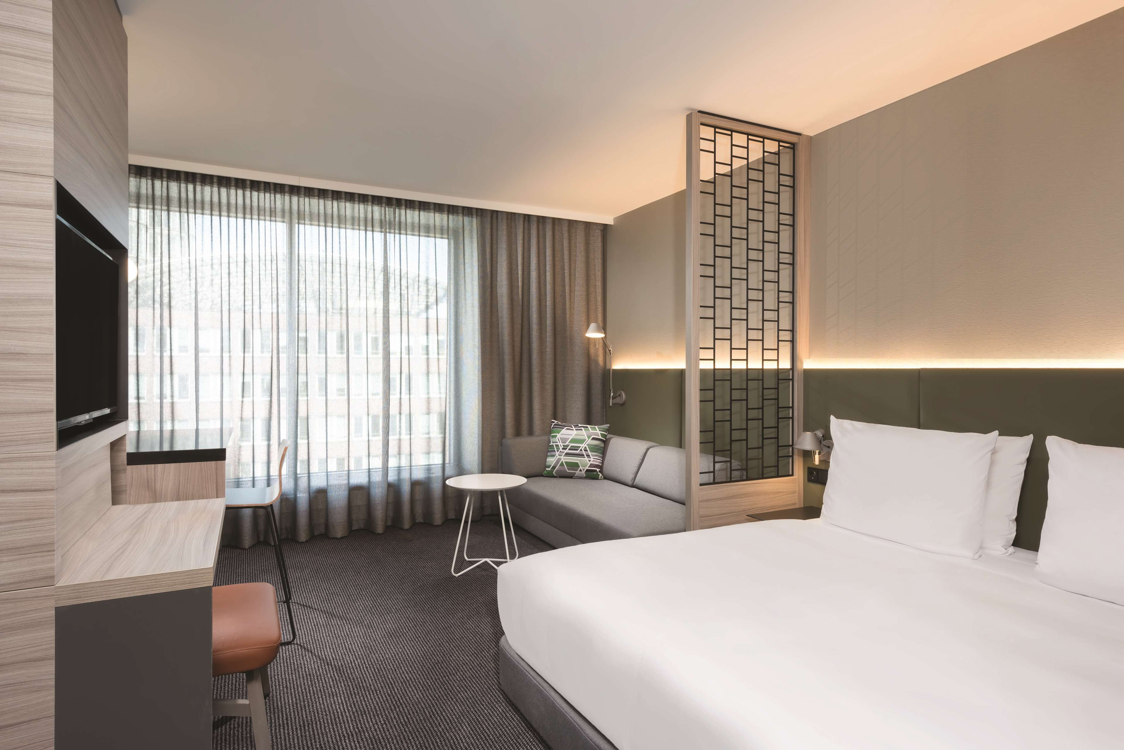 Quarto de hotel com uma cama grande, um sofá, uma mesa pequena, uma TV e um divisório decorativo.