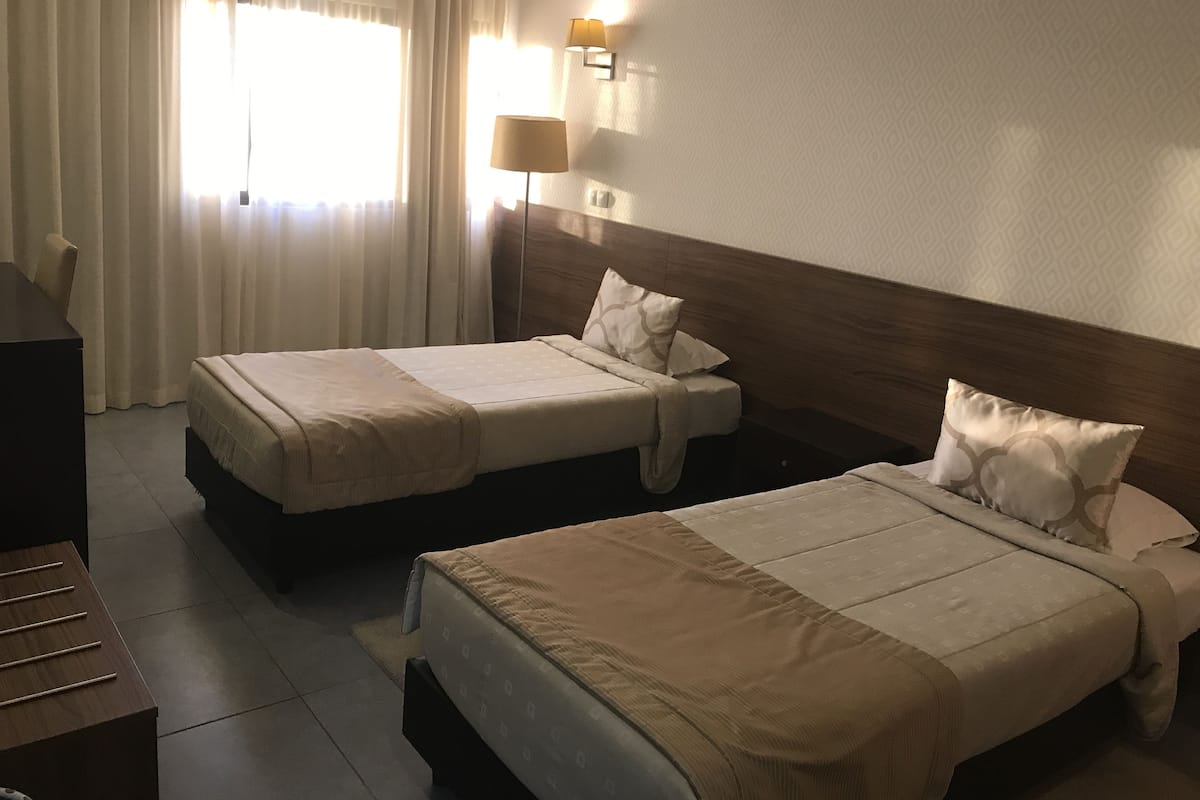 Quarto de hotel com duas camas, uma mesa e uma luminária.