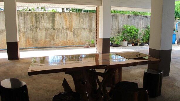 Um espaço amplo e interno com uma grande mesa de madeira, vários banquinhos e plantas em vasos.