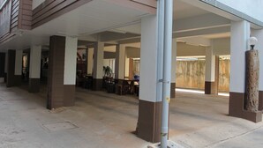 Amplo espaço coberto ao ar livre, com várias colunas, piso de concreto e vista do interior.