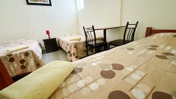 Quarto com duas camas de solteiro, uma cama grande, uma mesa com cadeiras, uma mesinha com abajur e um quadro na parede.