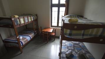 Quarto em dormitório com beliches, uma mesa pequena e uma janela.