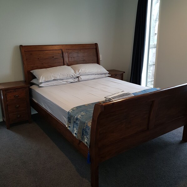 Uma cama de madeira com cabeceira, duas mesas de cabeceira e uma janela com cortinas.